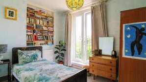 Um quarto com cama, estante, penteadeira, luminária globo, janela com cortinas e um pôster na parede.