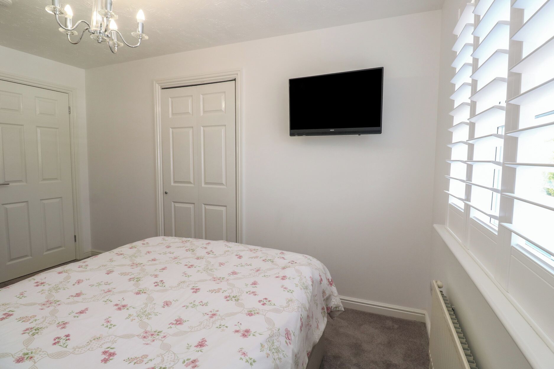 Quarto com cama, televisão na parede e janela com persianas.