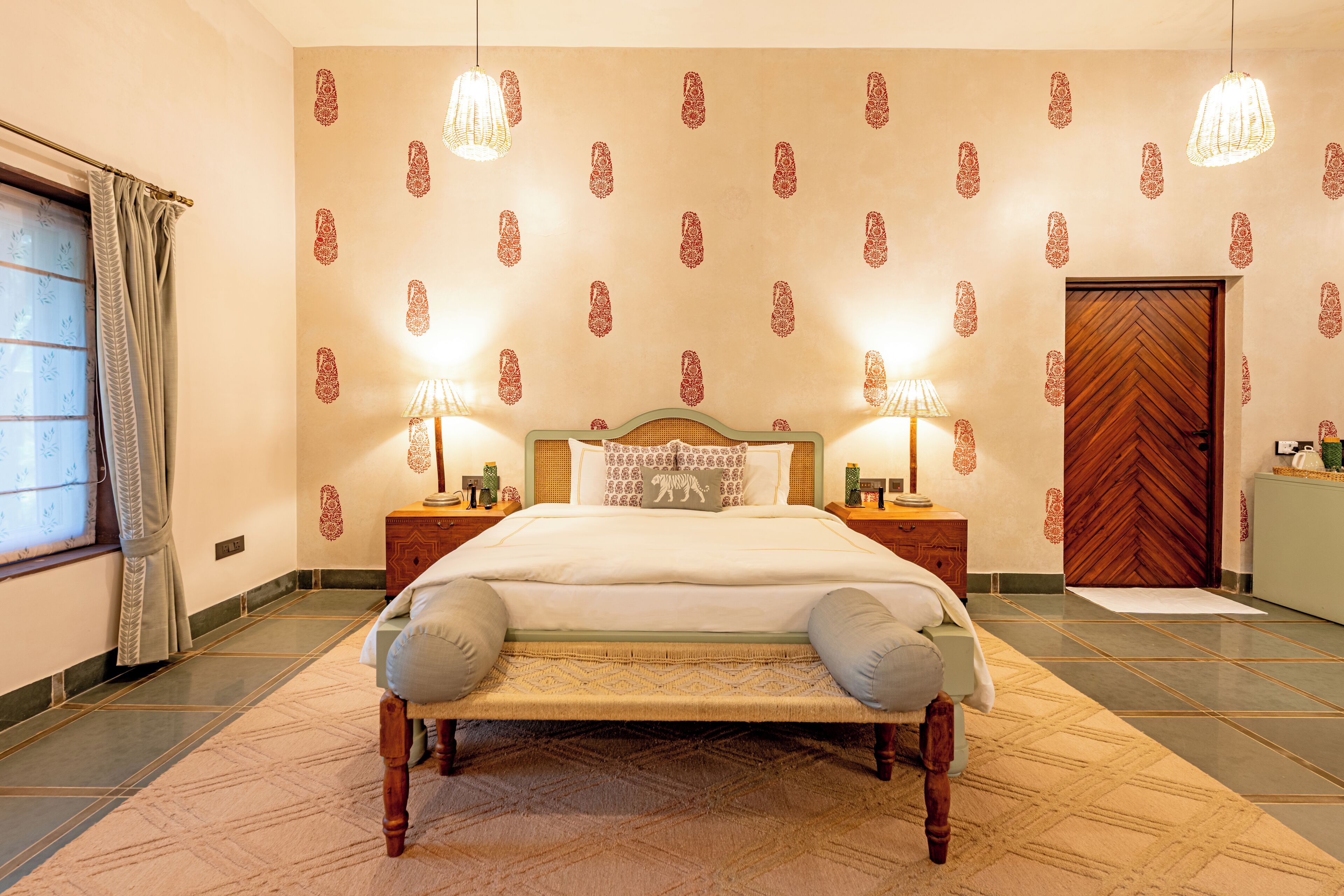 Quarto com uma cama grande, duas mesas de cabeceira, uma porta de madeira e papel de parede estampado.