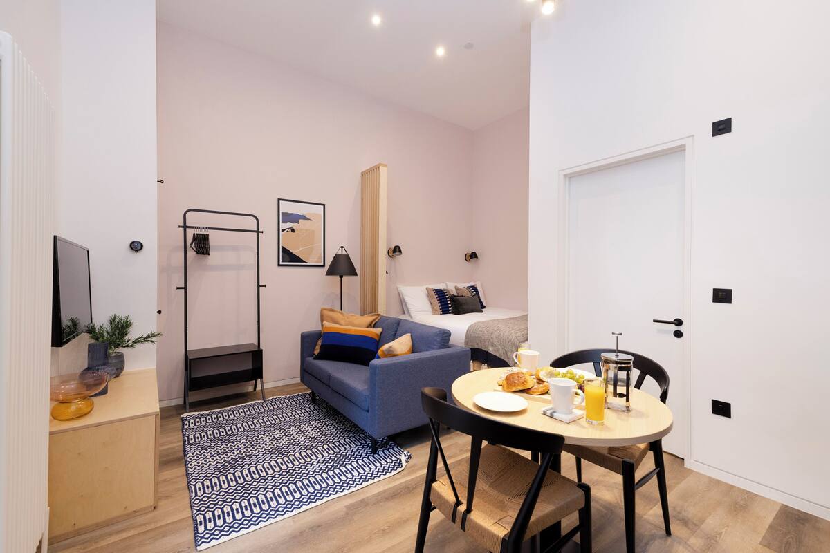 Um espaço de estar moderno e compacto, com sofá, mesa de jantar, pequena cozinha e cama.
