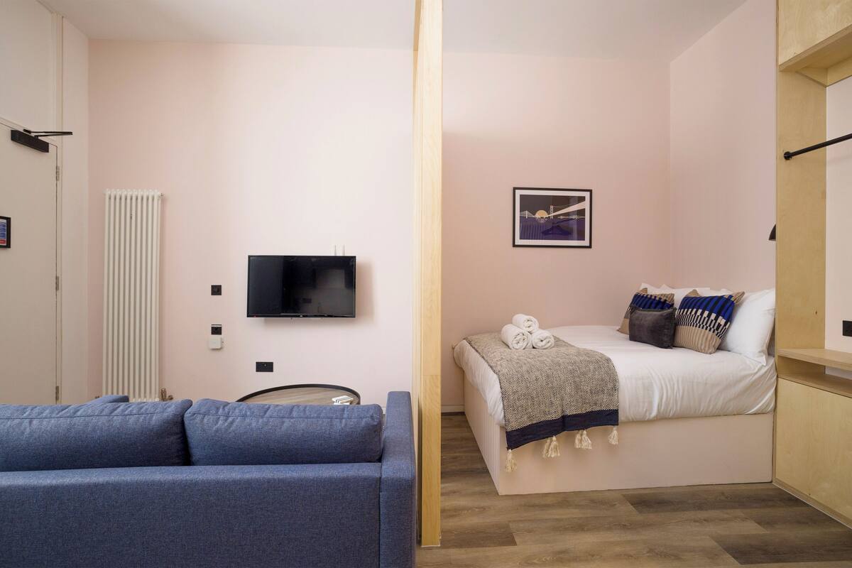 Quarto moderno com cama, sofá azul, televisão e radiador.