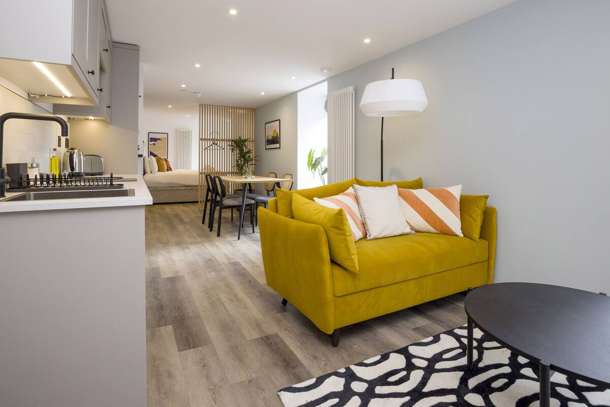 Um espaço de estar moderno com um sofá amarelo, uma área de jantar e uma cozinha com pia e fogão.