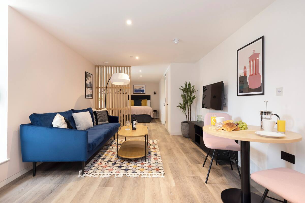 Uma sala de estar moderna com um sofá azul, uma mesa de centro e um espaço de jantar com mesa e cadeiras.