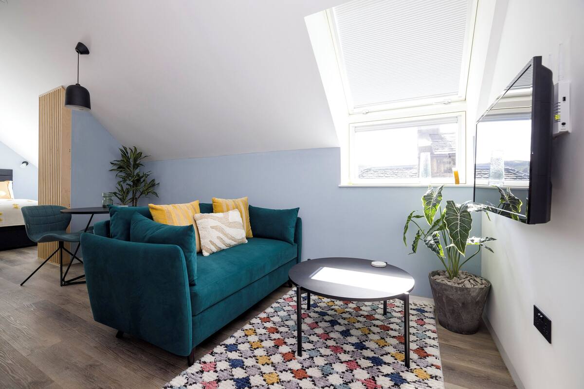 Uma sala de estar moderna com um sofá verde-água, uma mesa redonda pequena e uma planta grande em vaso.
