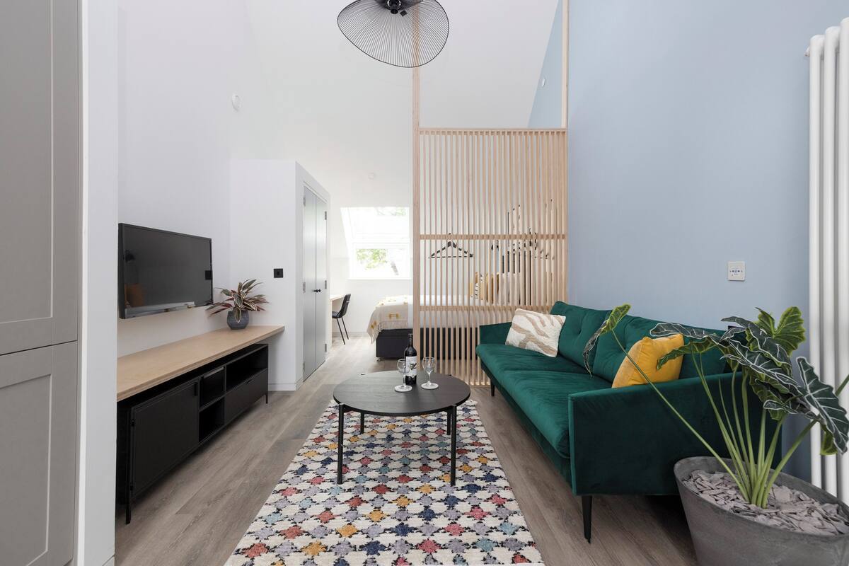 Uma sala de estar moderna com um sofá verde, uma mesa de centro, uma TV sobre um console de madeira e uma planta em vaso.