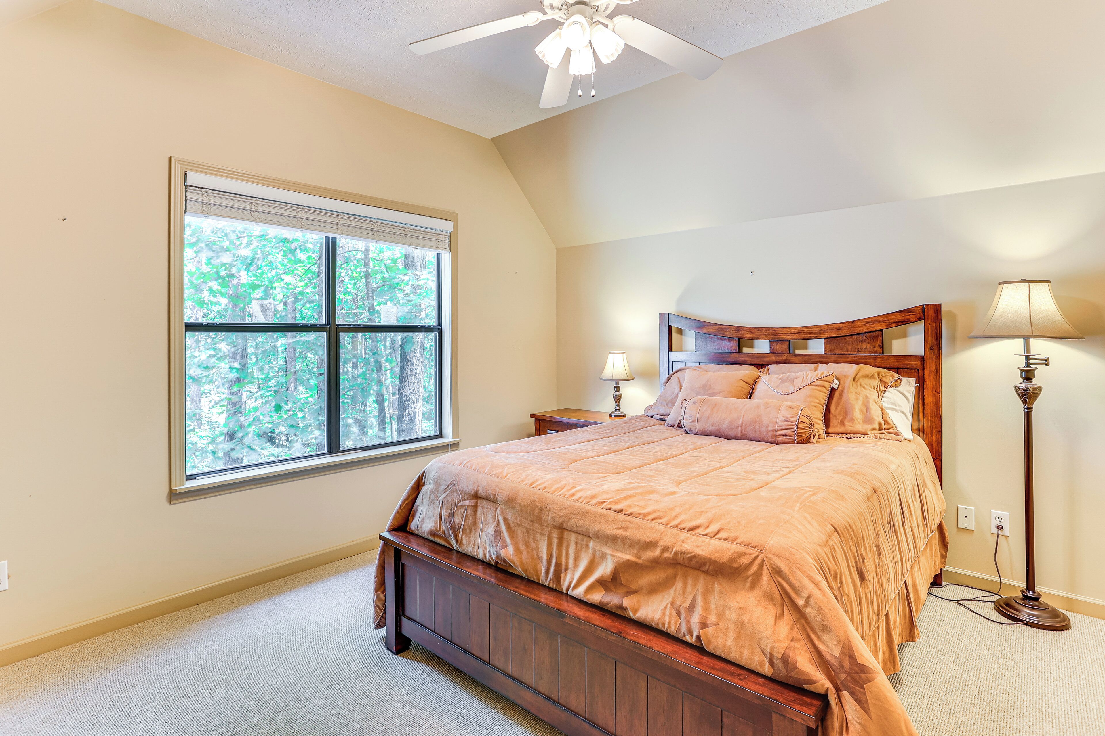 Quarto com uma janela grande, cama de madeira, duas luminárias de cabeceira e ventilador de teto.