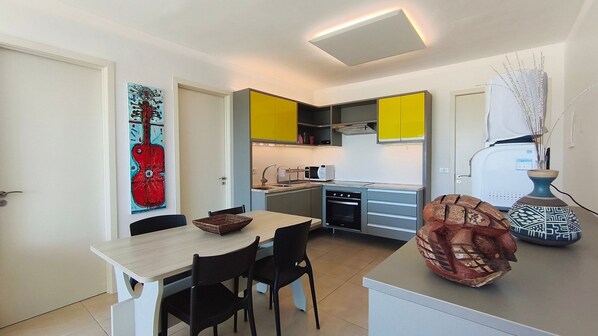 Cozinha compacta com eletrodomésticos modernos, área de refeições com mesa e cadeiras, e um vaso decorativo no balcão.