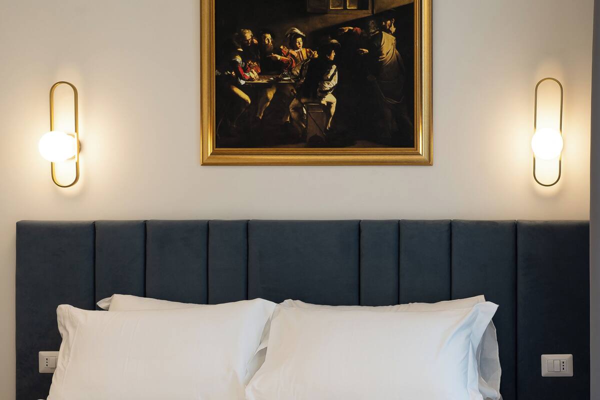 Uma cama bem arrumada com lençóis brancos, uma cabeceira escura e um quadro emoldurado acima.