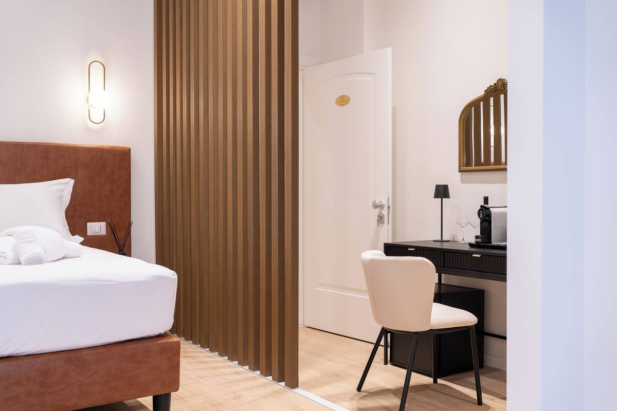 Quarto de hotel moderno com cama, escrivaninha, cadeira, espelho e porta.