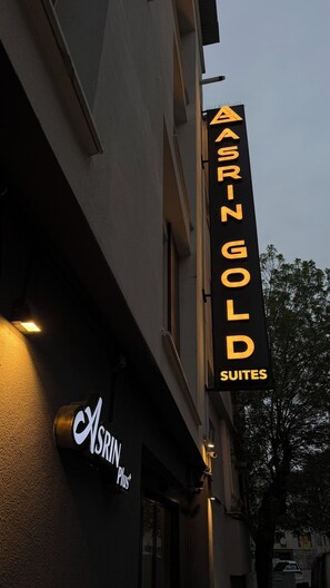 Um edifício com uma placa que diz 'ASRIN GOLD SUITES' e outra placa abaixo com a inscrição 'ASRIN Plus'.