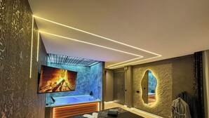 Quarto moderno com cama grande, TV fixada numa parede texturizada, parede de pedra com arco e um banco de madeira.