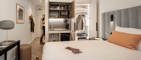 Quarto de hotel moderno com uma cama grande, uma escrivaninha, um guarda-roupa e uma kitchenette.