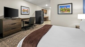 Quarto de hotel com cama, escrivaninha, cadeira, televisão, frigorífico e quadros nas paredes.