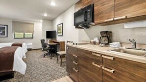 Quarto de hotel com cama, escrivaninha com cadeira, micro-ondas, máquina de café e pia.