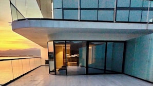 Um interior espaçoso e moderno, com uma área aberta ampla, uma parede de vidro com vista para o pôr do sol e um detalhe arquitetônico curvo.