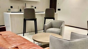 Cozinha moderna com ilha central, duas cadeiras cinzas, uma mesa redonda e um sofá marrom.