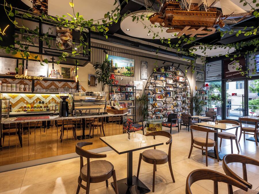 Interior de uma cafeteria com balcão, área de estar e uma grande estante de livros.