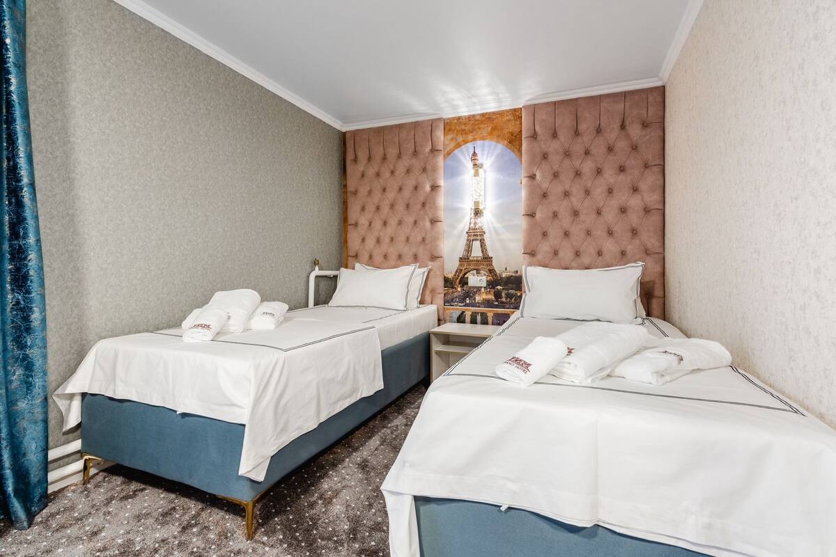 Quarto de hotel com duas camas, vista da Torre Eiffel pela janela e cabeceira estofada.