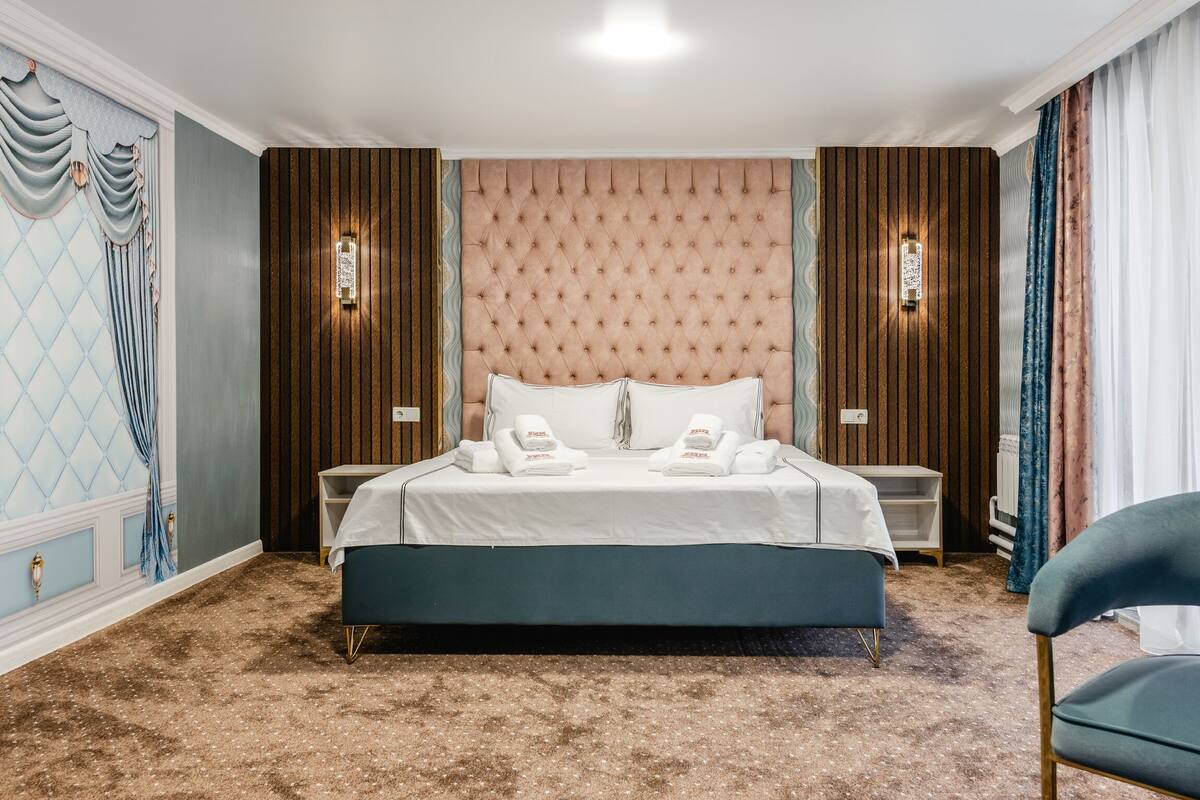 Quarto bem arrumado com cabeceira estofada, uma cama grande com roupa de cama branca, duas mesas de cabeceira e uma cadeira.