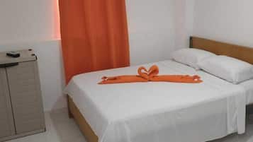 Quarto individual com uma cama de solteiro, cabeceira de madeira, roupa de cama branca, uma toalha laranja sobre a cama, um guarda-roupa de madeira e uma cadeira laranja.