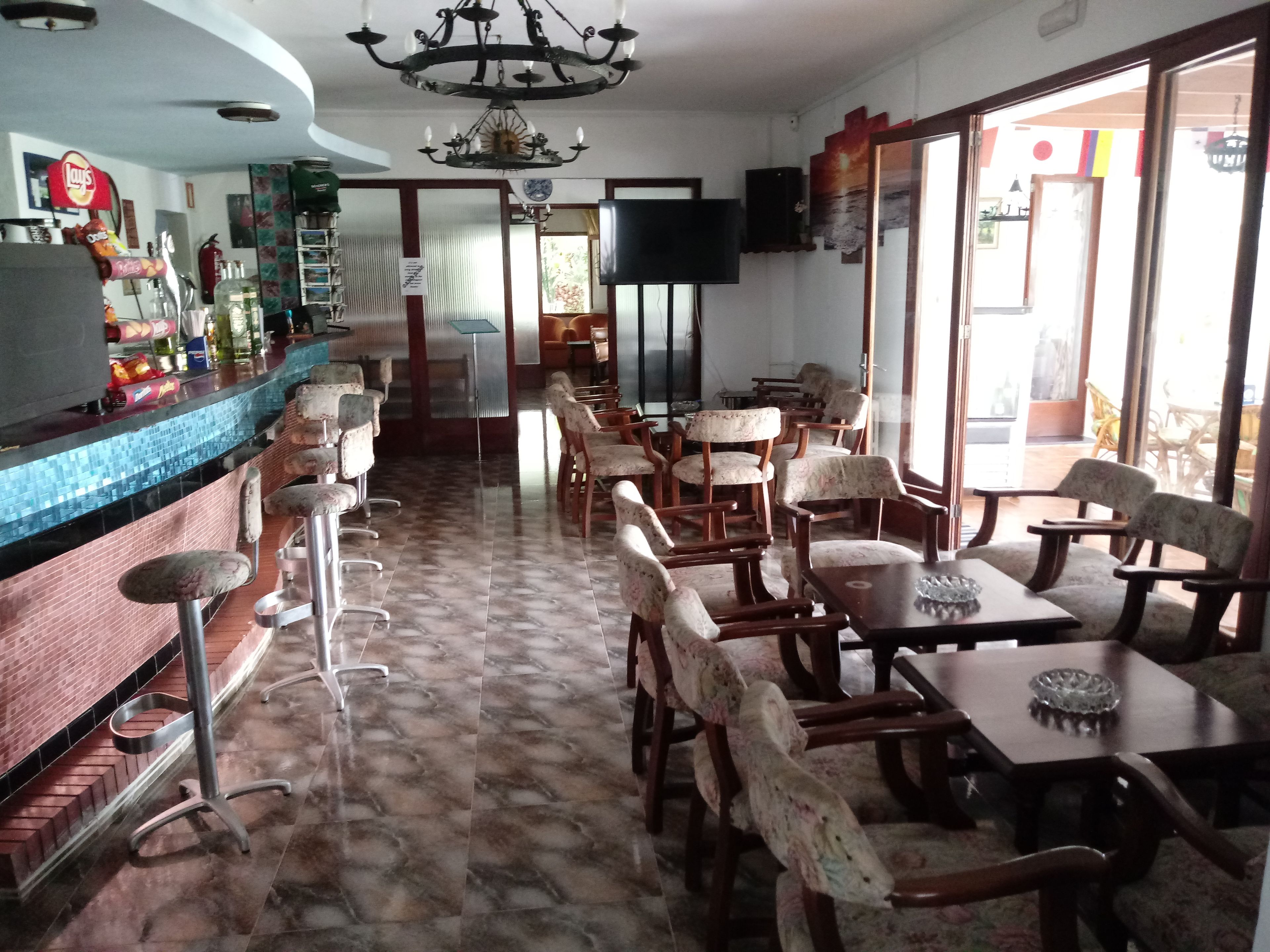 Um restaurante com área de bar, diversas opções de assento incluindo banquetas e mesas, um lustre e uma televisão na parede.