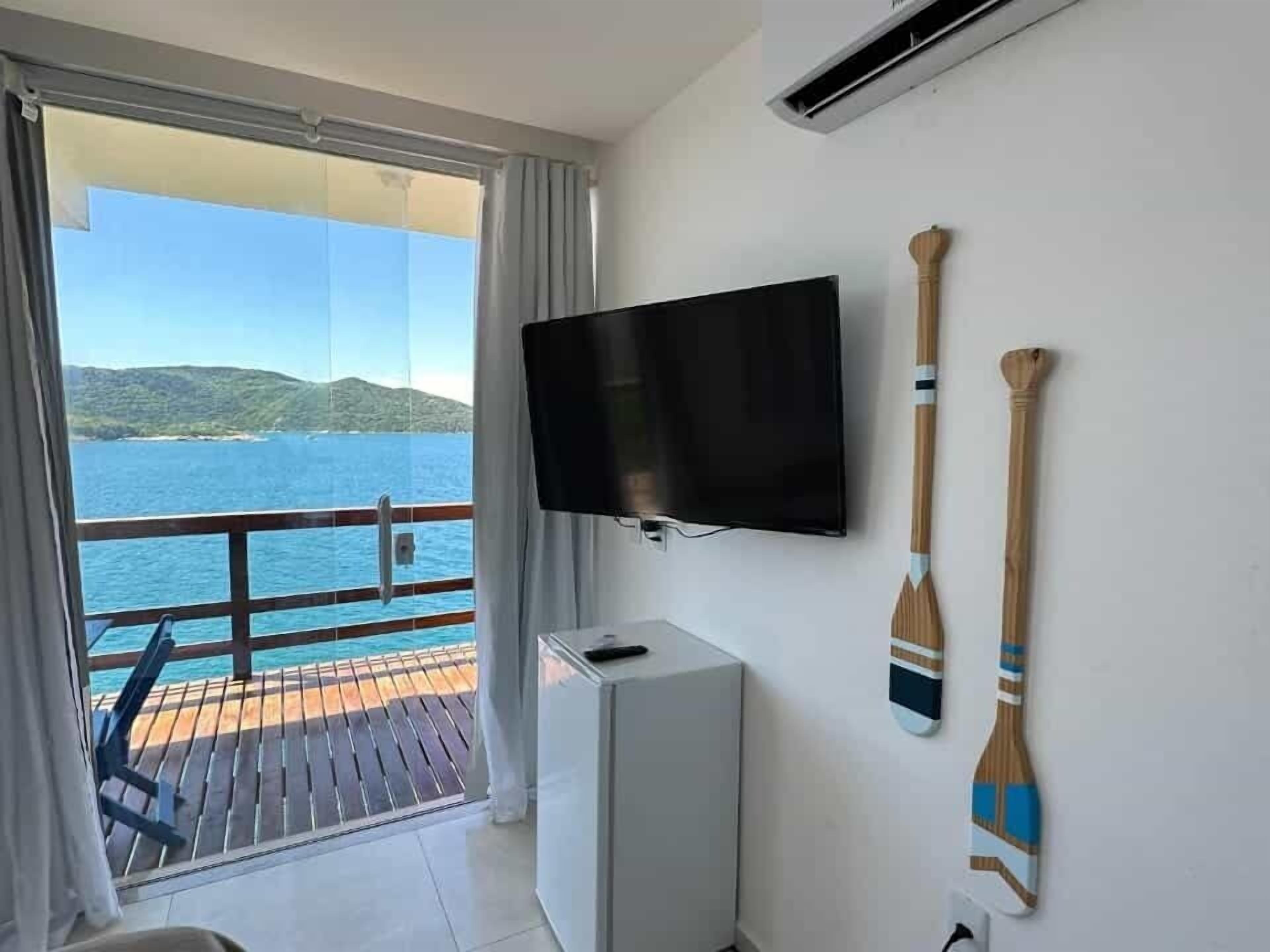 Quarto com televisão na parede, um pequeno armário branco e dois remo de madeira pendurados na parede.