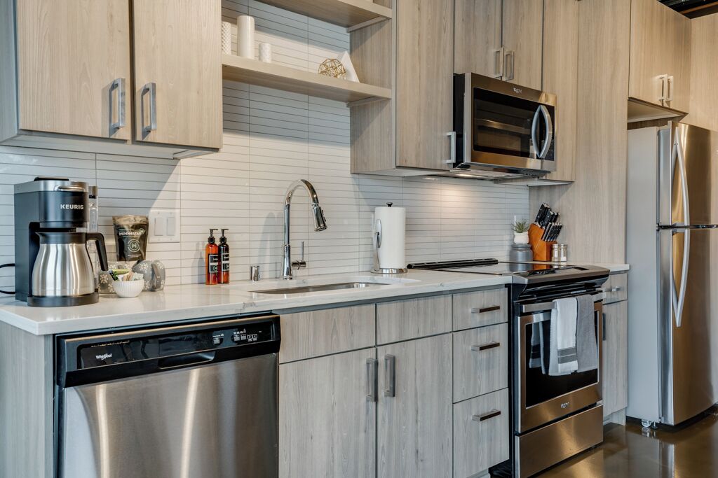 Uma cozinha moderna com eletrodomésticos de aço inoxidável, armários de madeira e painel de azulejos branco.