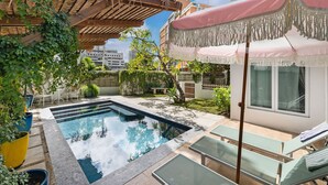 Piscina com espreguiçadeiras, pérgola com plantas trepadeiras e área de estar coberta.