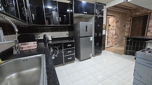 Uma cozinha com armários pretos, uma geladeira de aço inoxidável e piso de azulejos.