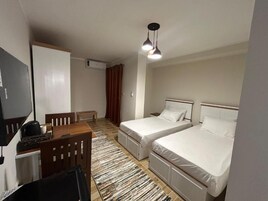 Quarto de hotel com duas camas, uma escrivaninha com cadeira, televisão e luminária no teto.