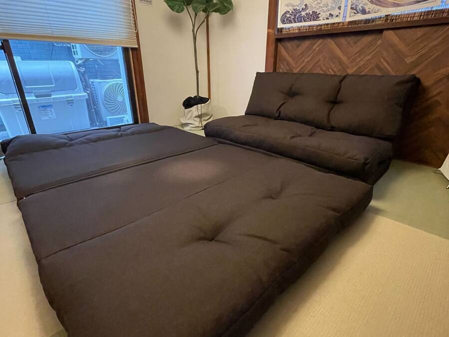 Um quarto com uma cama, uma janela com persianas, um vaso de plantas e uma parede com obras de arte.