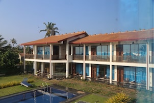 Um hotel de dois andares com piscina, área de estar externa e vista para palmeiras.