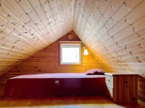 Um quarto de sótão pequeno, com telhado inclinado, uma janela, cama, penteadeira e abajur.