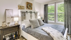 Quarto com cama, mesas de cabeceira, cômoda e janela com cortinas.