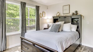 Quarto com cama grande, cômoda, mesa de cabeceira e janela com cortinas.