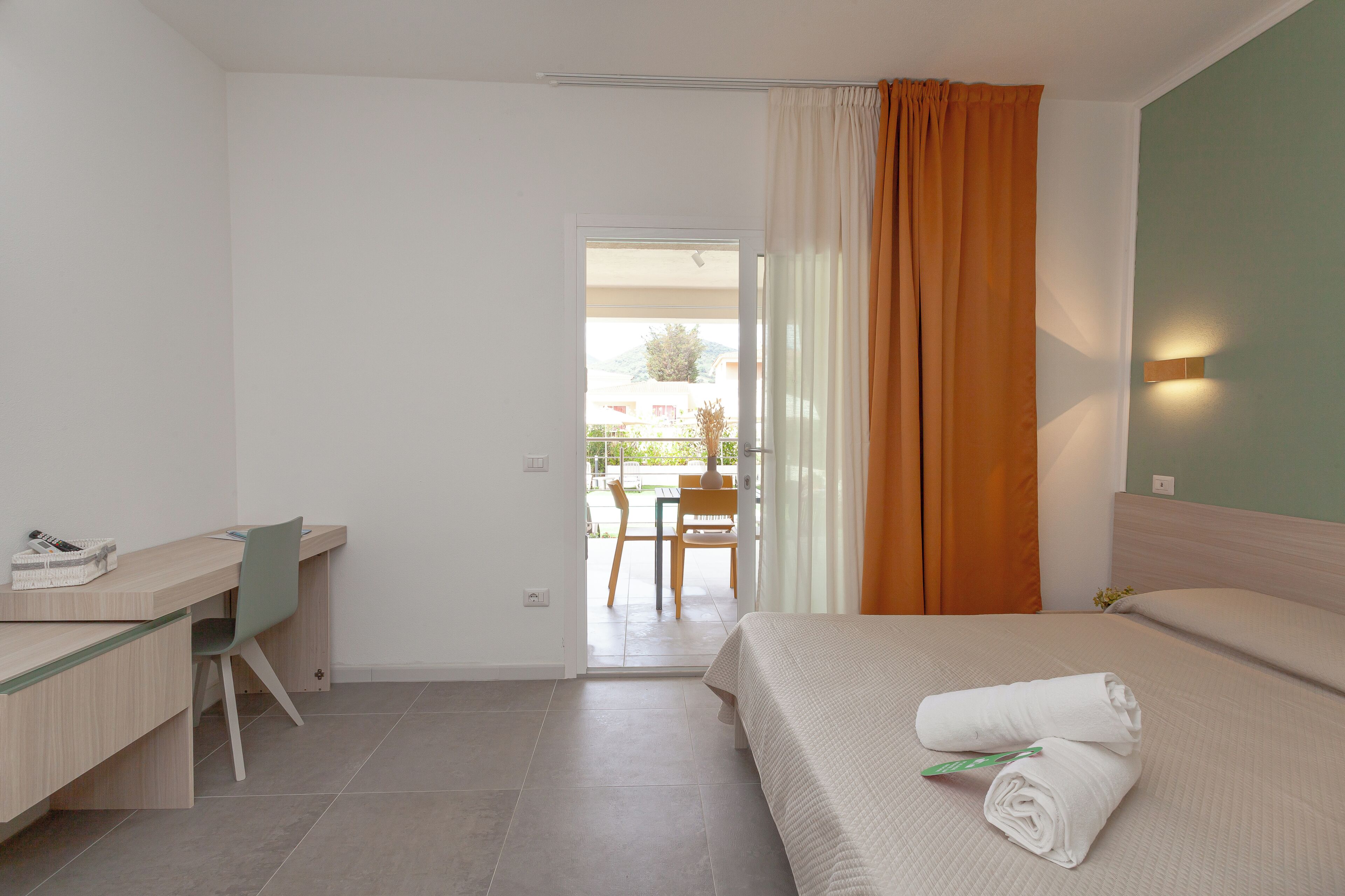 Quarto de hotel com cama, escrivaninha, cadeira e vista para o exterior.