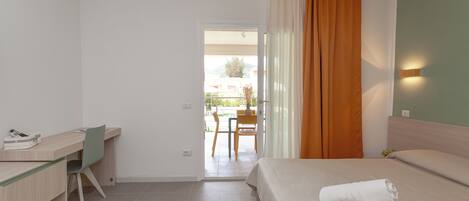 Quarto de hotel com cama, escrivaninha, cadeira e vista para o exterior.