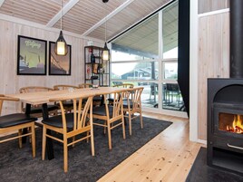 Uma área de refeições com mesa e cadeiras de madeira, lareira e uma grande janela com vista para o exterior.