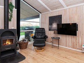 Uma sala de estar moderna com lareira, uma poltrona de couro confortável, uma TV de tela plana e uma janela grande com vista para o exterior.