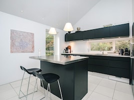 Uma cozinha moderna com uma ilha central, banquetas pretas, iluminação pendente e uma janela ampla.