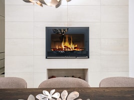 Uma lareira moderna com uma tela de TV, uma mesa de jantar com cadeiras e um objeto decorativo na parede.