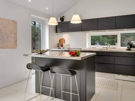 Uma cozinha moderna com uma ilha central, dois banquetes, iluminação pendente e uma janela grande.