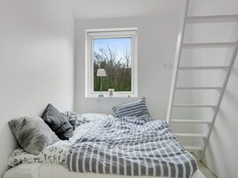 Um quarto com cama, travesseiros, janela e uma escada.