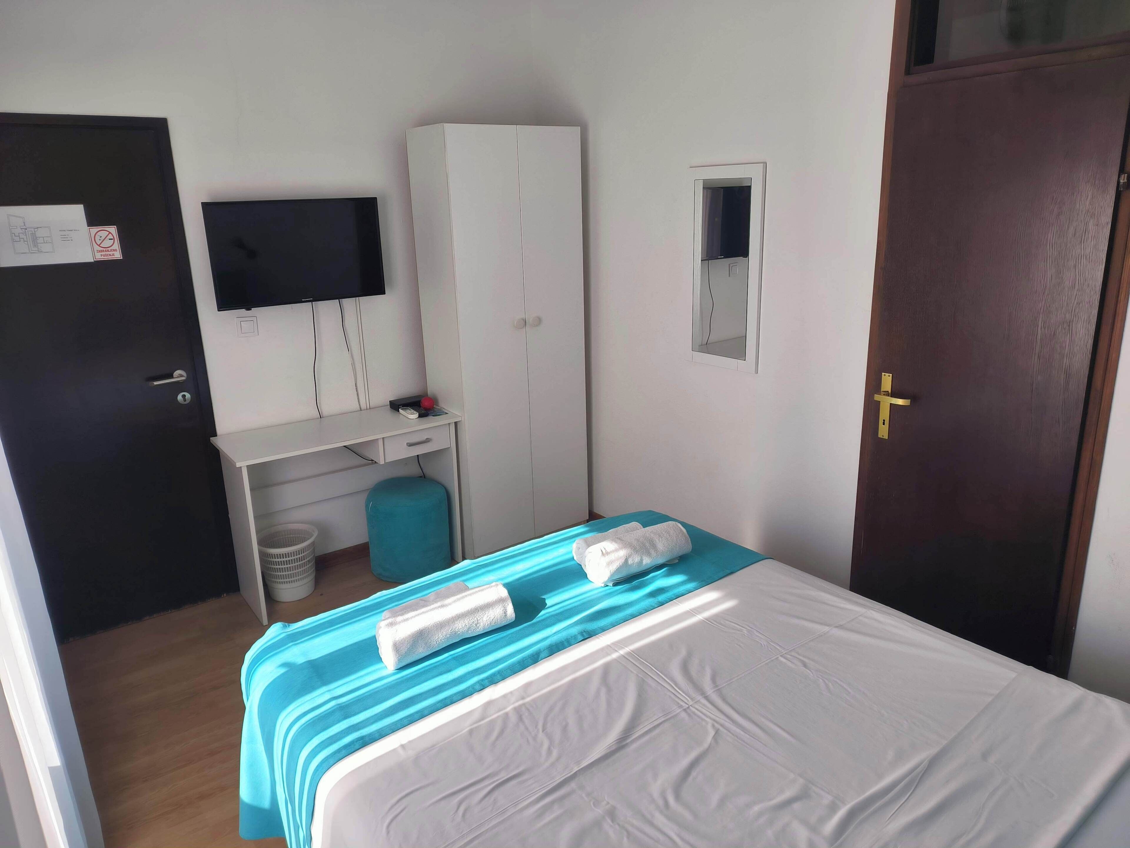 Quarto com cama, escrivaninha, guarda-roupa e televisão.