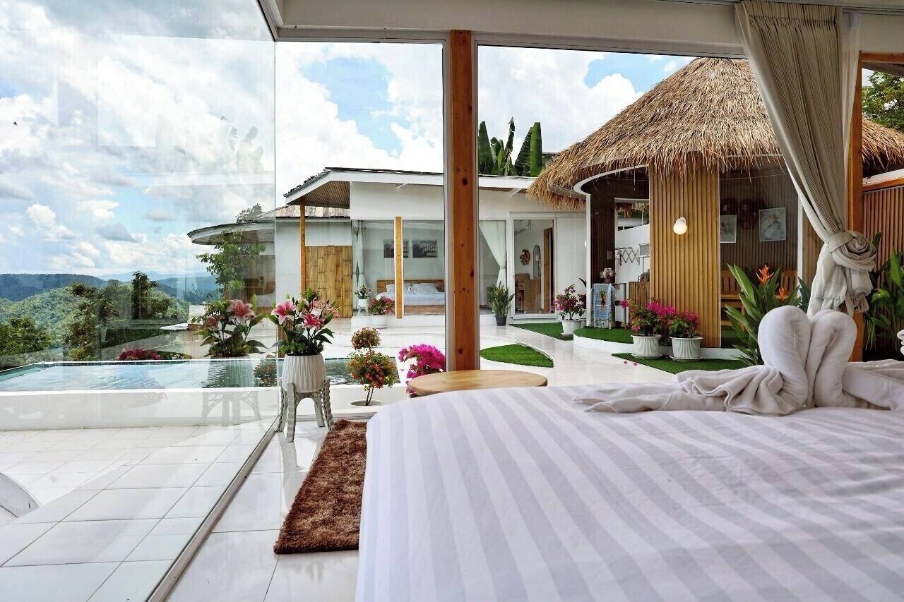 Quarto moderno com uma cama grande, varanda envidraçada e vista para uma piscina e montanhas.