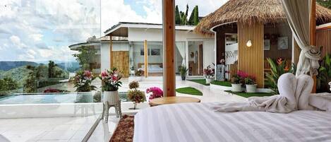 Quarto moderno com uma cama grande, varanda envidraçada e vista para uma piscina e montanhas.