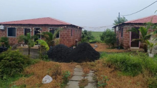 Cenário rural com duas casas de tijolo e telhados de terracota, rodeadas por vegetação e um caminho de terra.