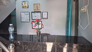 Um balcão de recepção com bancada de mármore, certificados emoldurados e um vaso com uma flor vermelha.