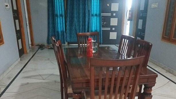 Uma área de jantar com uma mesa de vidro cercada por cadeiras de madeira, cortinas azuis e piso de azulejos.