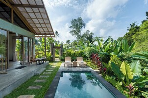 Uma área de piscina com espreguiçadeiras e um deck de madeira, cercada por vegetação tropical exuberante.